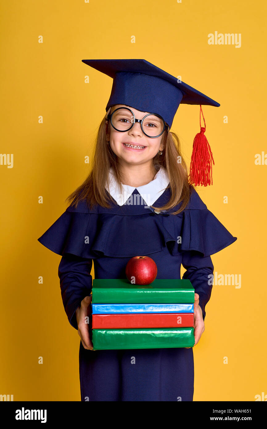 School Girl in academician clothes with book and apple on yellow stduio ...