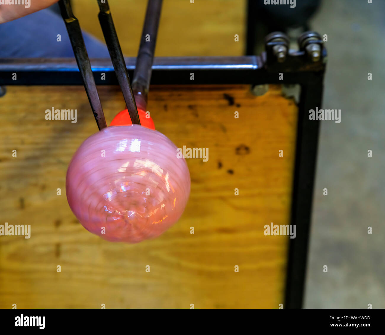 Glass blower shaping a bubble of melted glass on a rod by hand in the ...