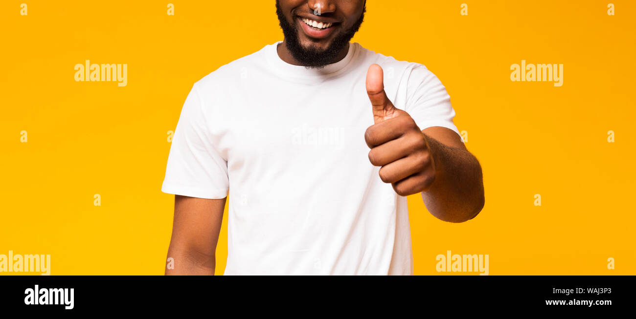 Pleased man showing thumb up, smiling broadly over yellow background ...