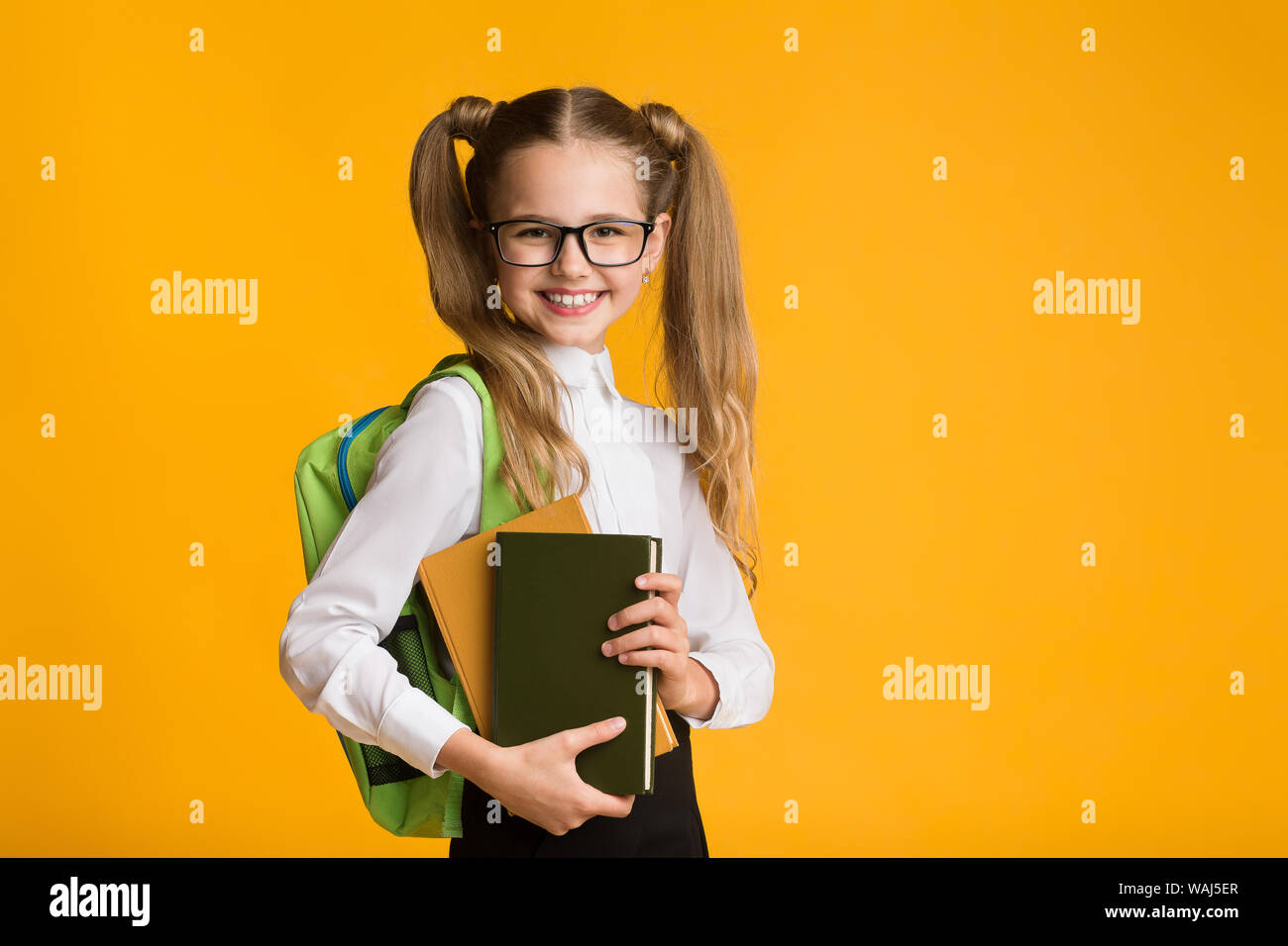 Smiling Elementary School Girl Holding Books Posing Over Yellow ...