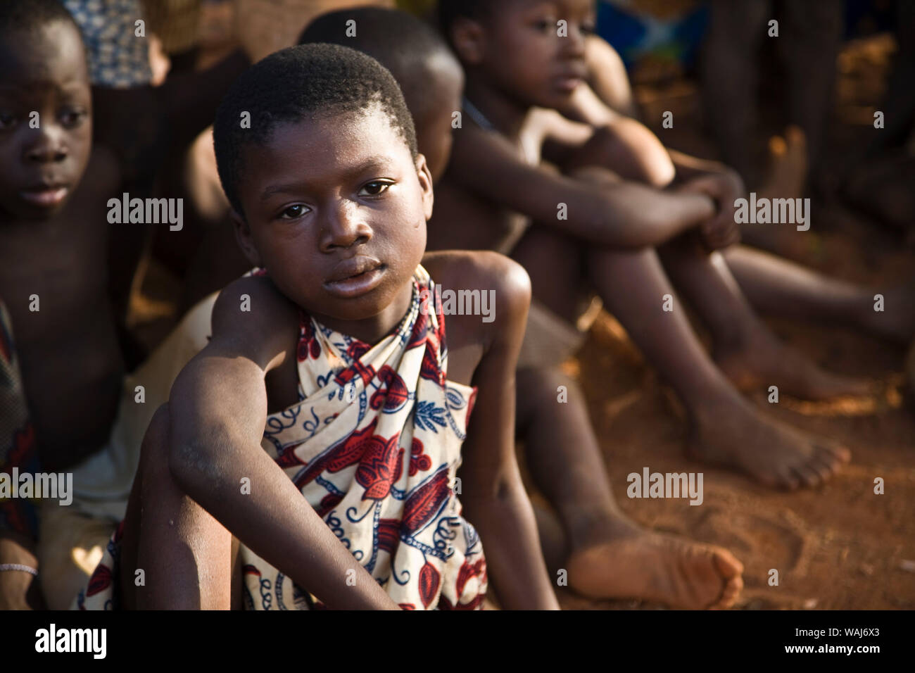 West Africa, Benin. Young girl sits in sunlight surrounded by youth ...