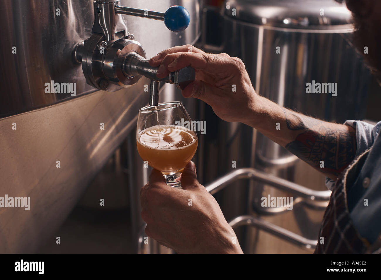 Bartender with a tattoo on his arm pours beer from the tap into the big ...