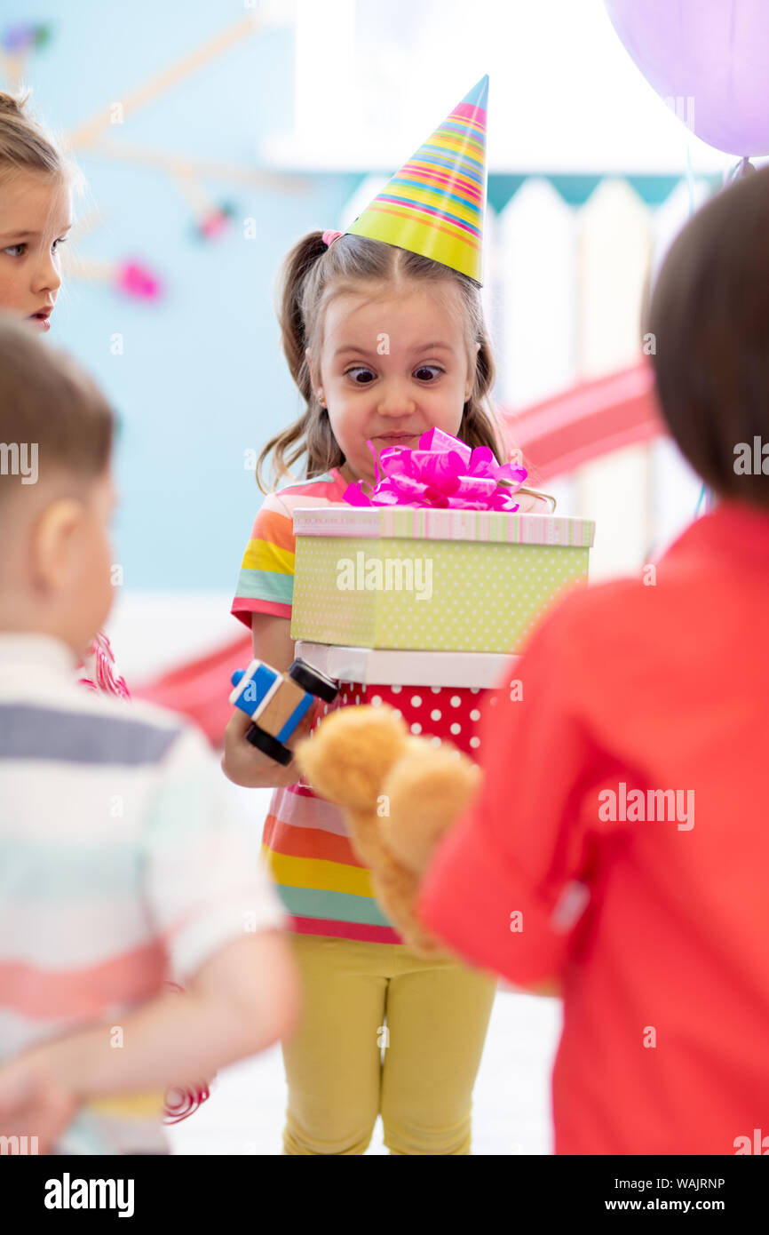 Surprised kid girl taking from friends gifting boxes indoors. Funny ...