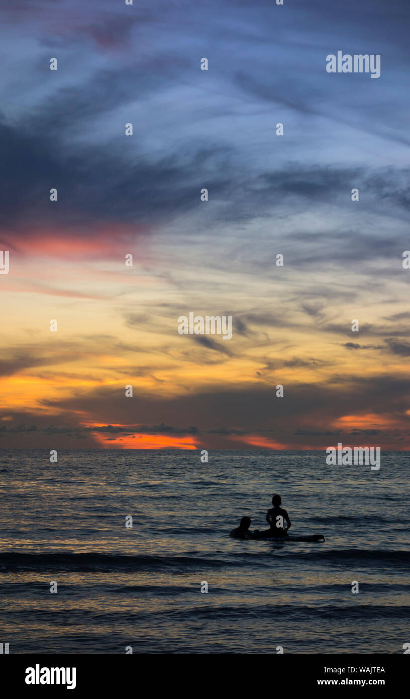 Two boys sitting on wakeboard, watching sunset Stock Photo - Alamy