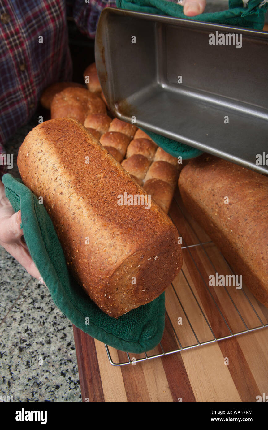 Woman removing loaf of just baked multigrain bread from bread pan. (MR ...