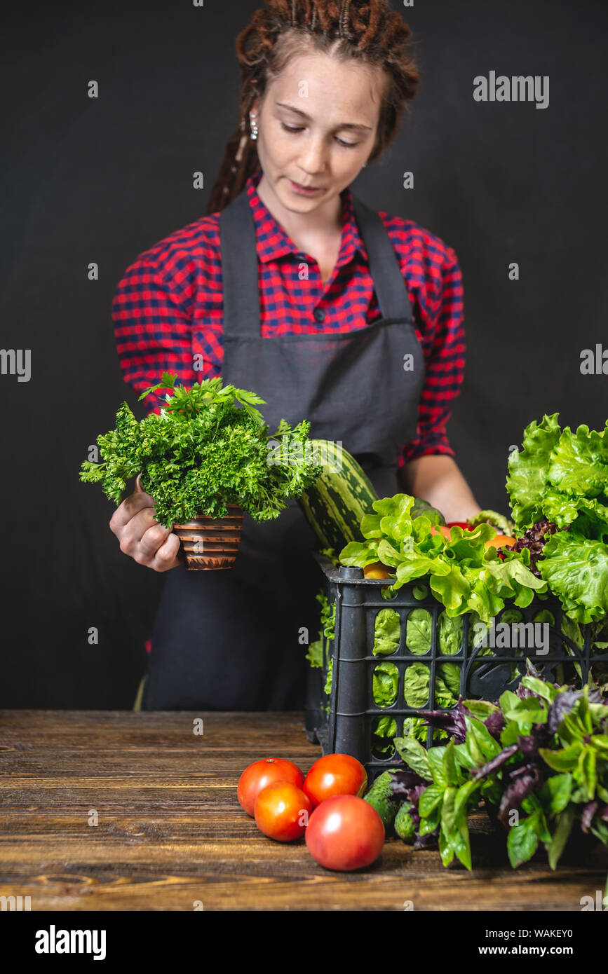 A young woman farmer is holding a box with fresh vegetables and green ...