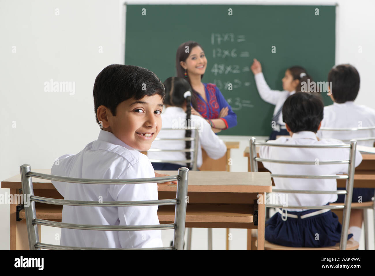 Schoolboy looking back towards camera and schoolgirl teaching her ...