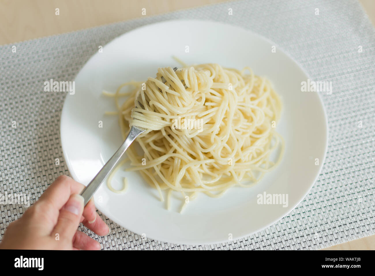 Spaghetti on a fork in the plate background. Woman fingers holding fork ...