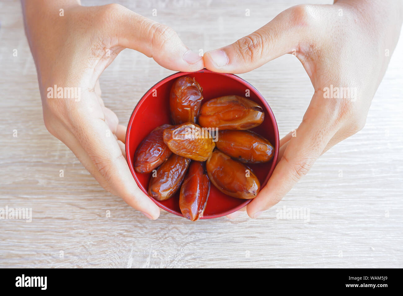 hand holding red bowl with dried fruits from date palm on wooden ...