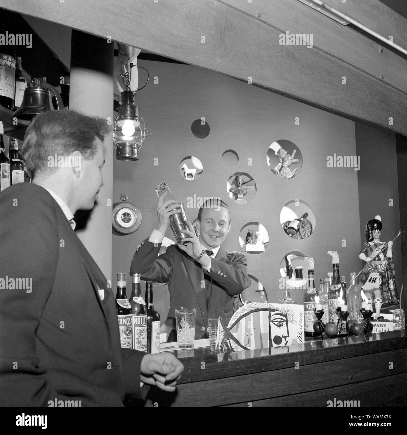 Bar in the 1950s. A bartender is mixing drinks behind the bar counter ...