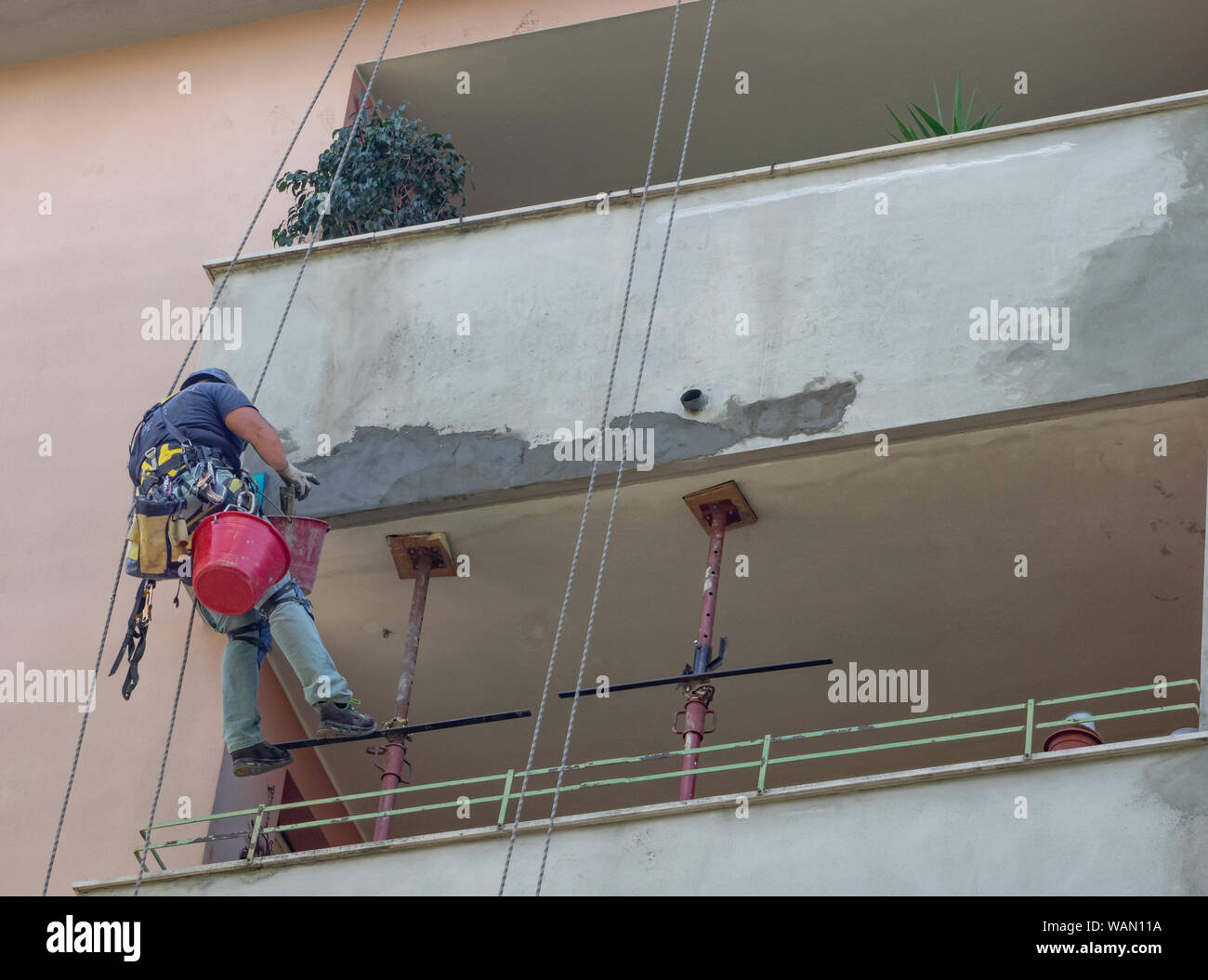 skilled worker repairs the facade of a building hanging from a rope ...