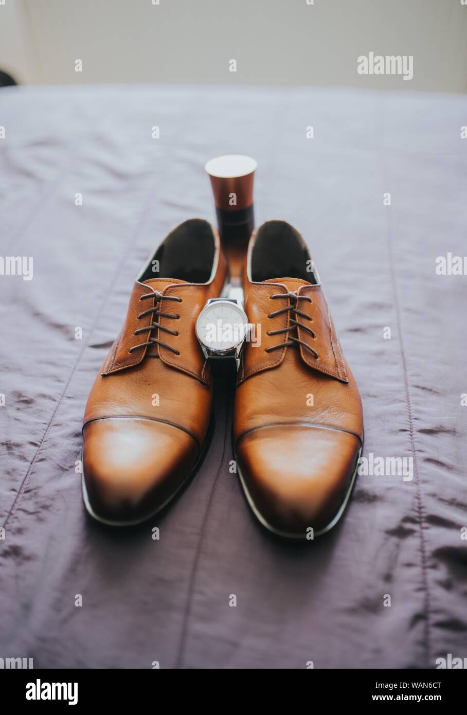 Vertical shot of brown classic shoes on a gray sheet with a watch in ...