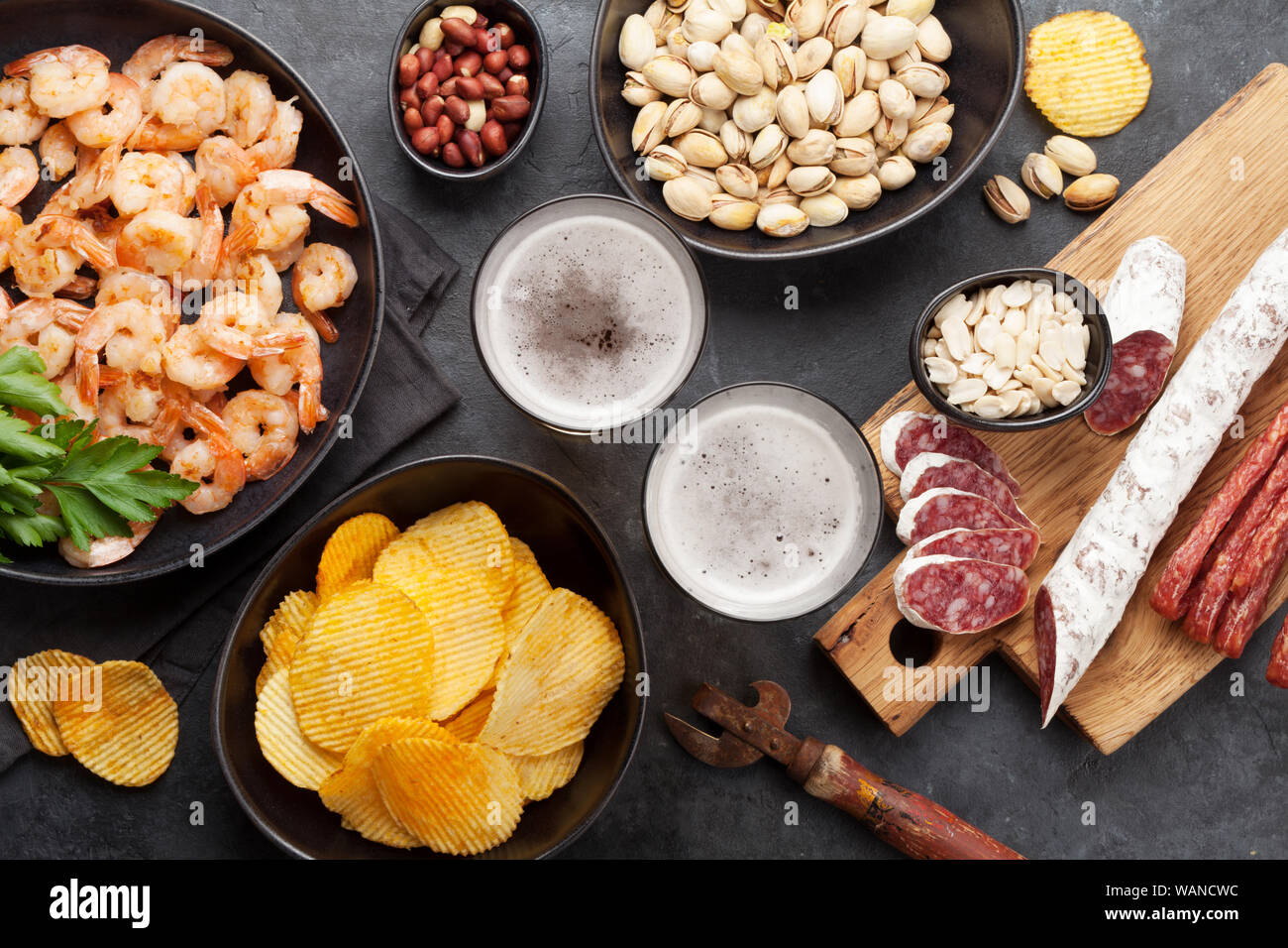 Draft beer and snacks on stone background. Nuts, chips, sausages and ...
