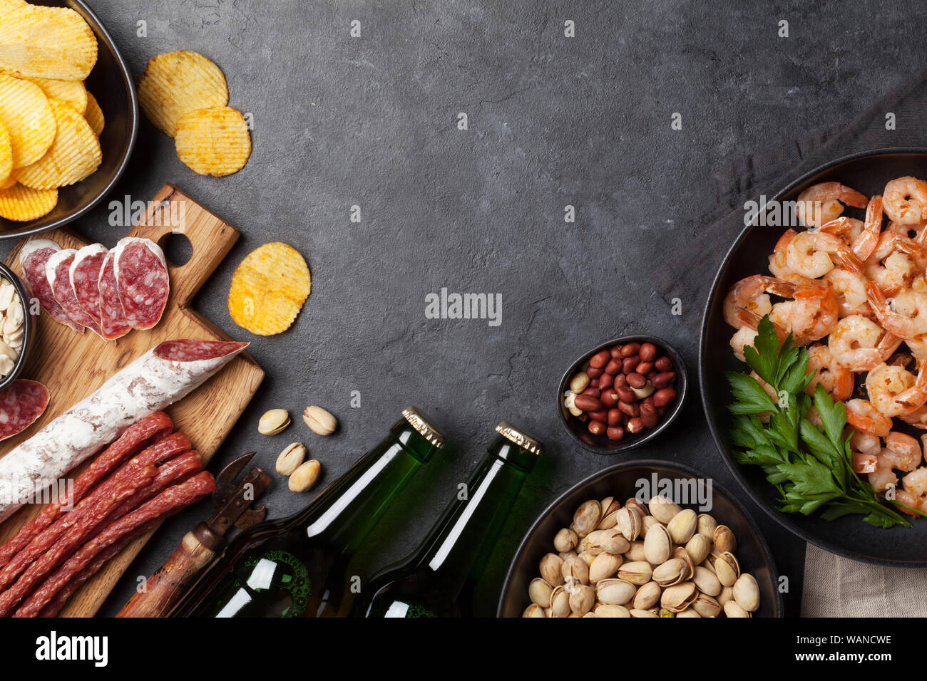 Draft beer and snacks on stone background. Nuts, chips, sausages and ...