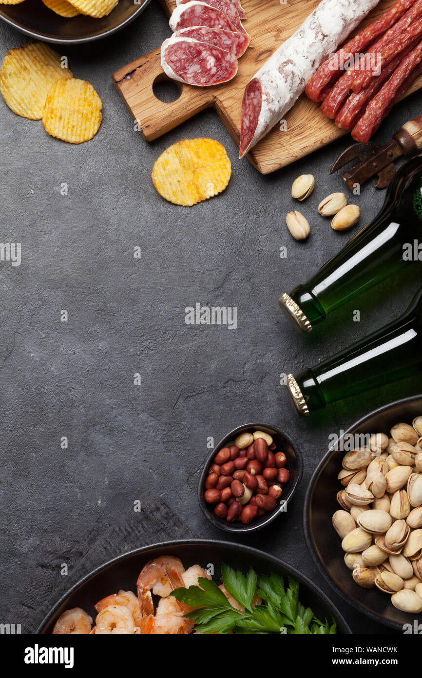 Draft beer and snacks on stone background. Nuts, chips, sausages and ...