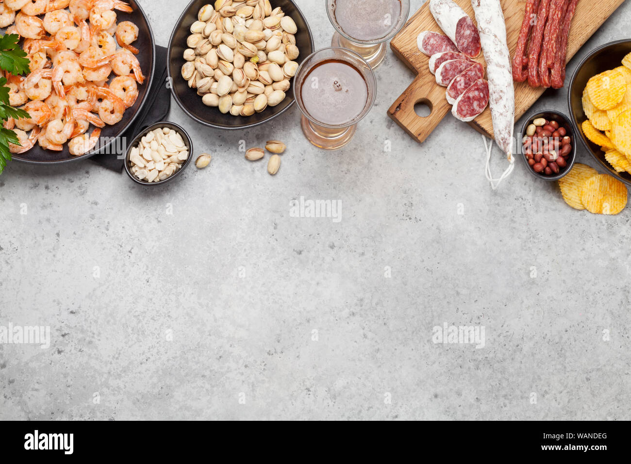 Draft beer and snacks on stone background. Nuts, chips, sausages and ...
