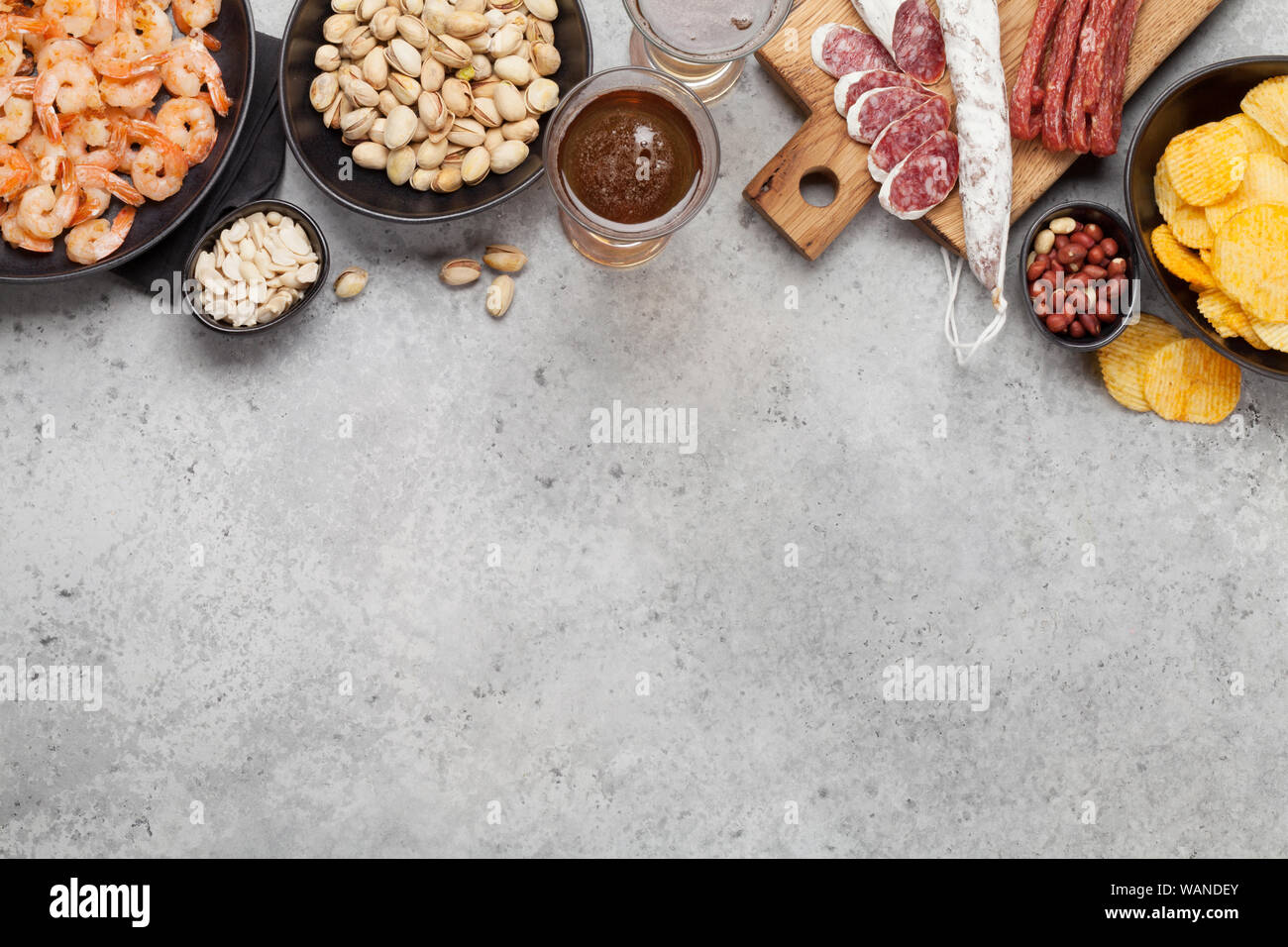 Draft beer and snacks on stone background. Nuts, chips, sausages and ...