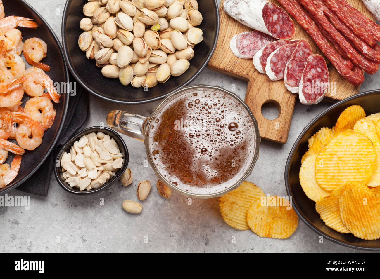 Draft beer and snacks on stone background. Nuts, chips, sausages and ...