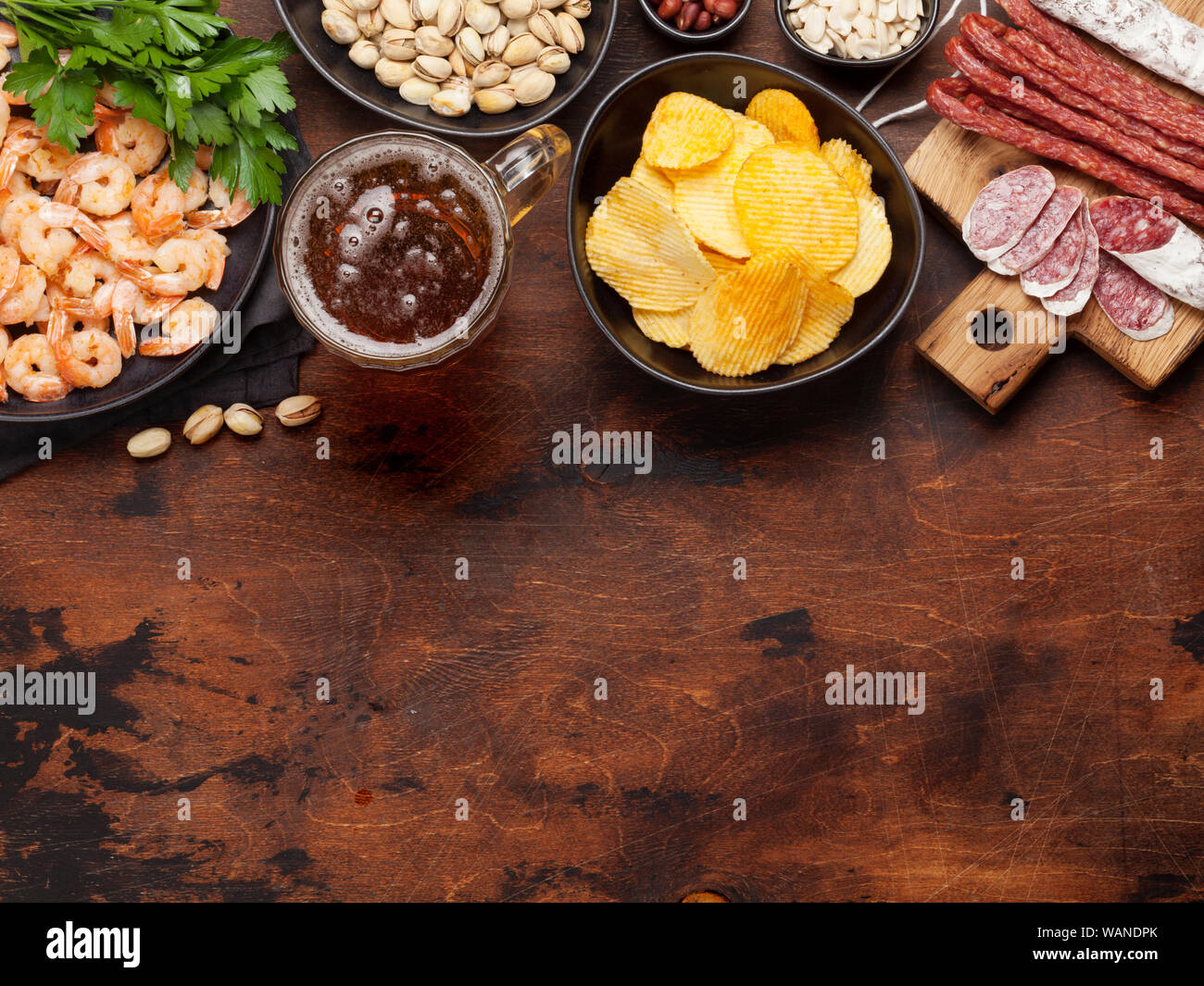 Draft beer and snacks on wooden background. Nuts, chips, sausages and ...