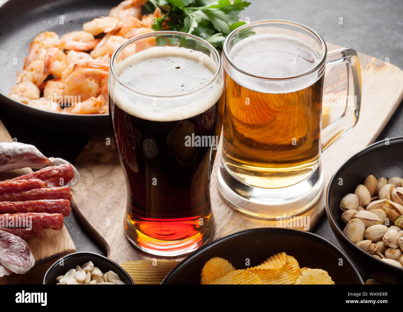 Draft beer and snacks on stone background. Nuts, chips, sausages and ...