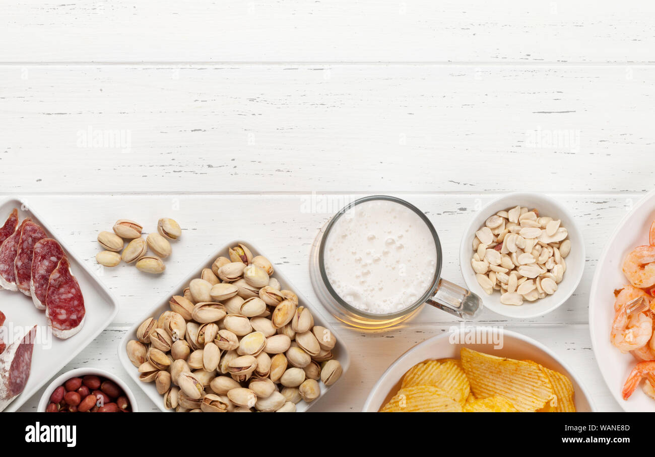 Draft beer and snacks on wooden background. Nuts, chips, sausages and ...