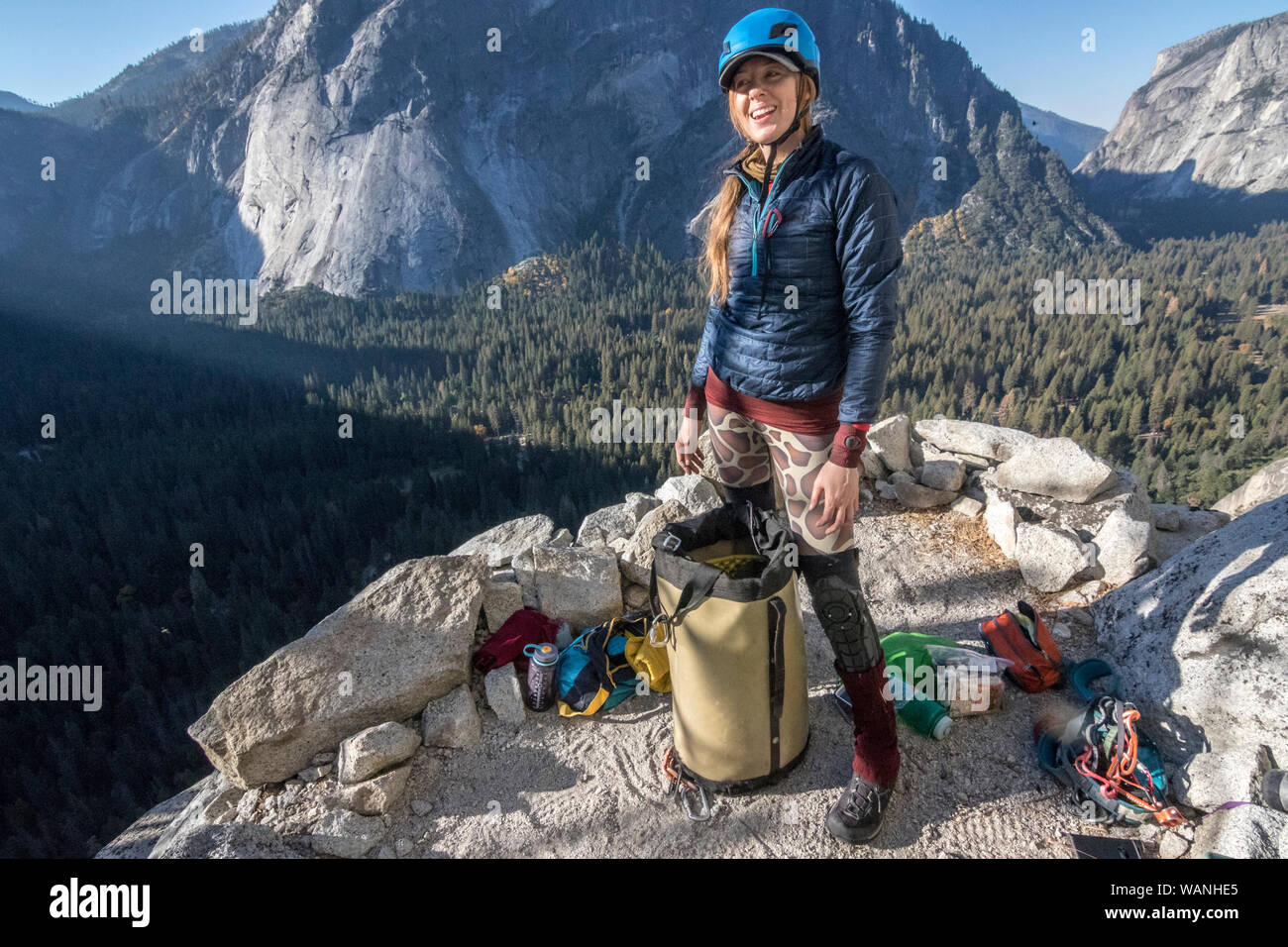 A young woman climber smiles as she stands on last night's bivy ledge ...
