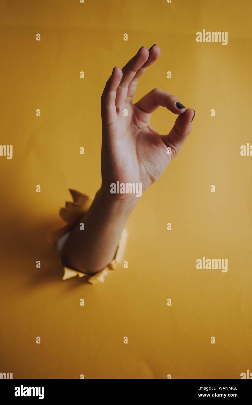Vertical shot of a person's hand breaking through a yellow paper wall ...