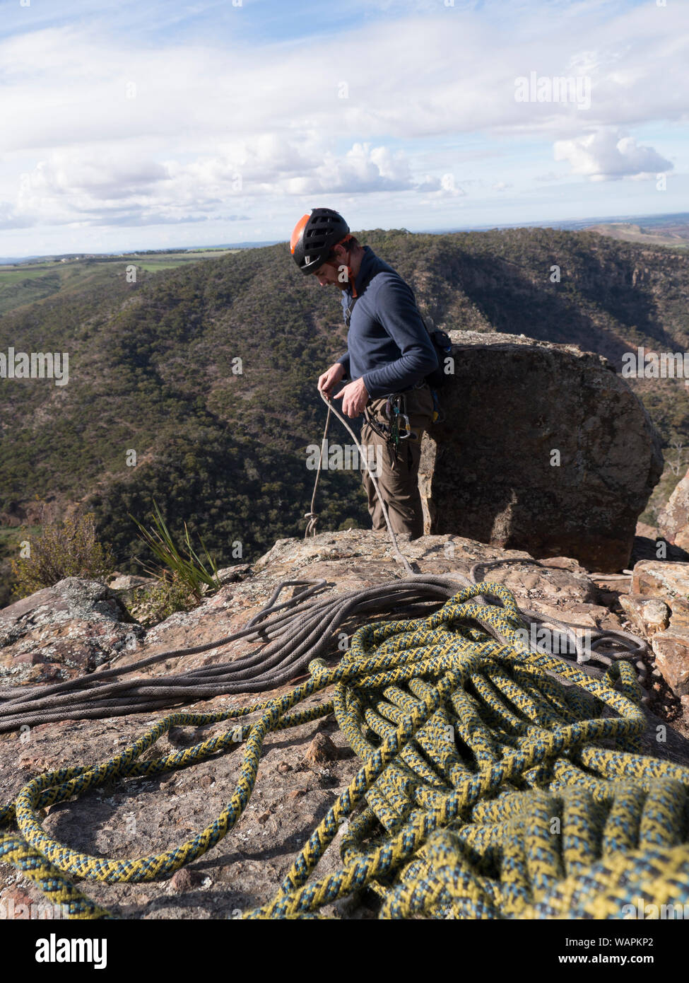 Technical climbing instructor inspecting and laying out rope on cliff ...