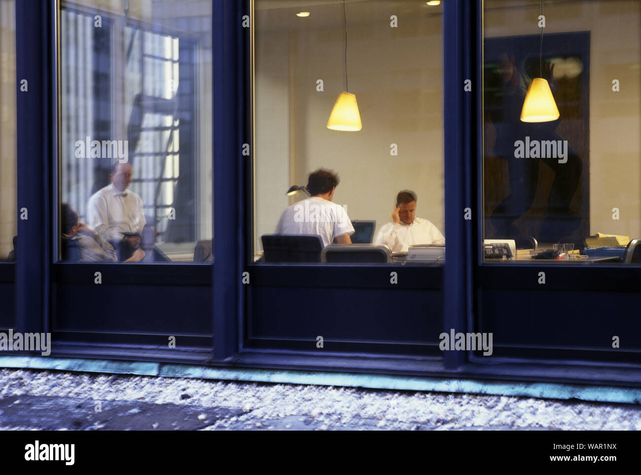 A small group of men are sitting inside a room with glass windows Stock ...