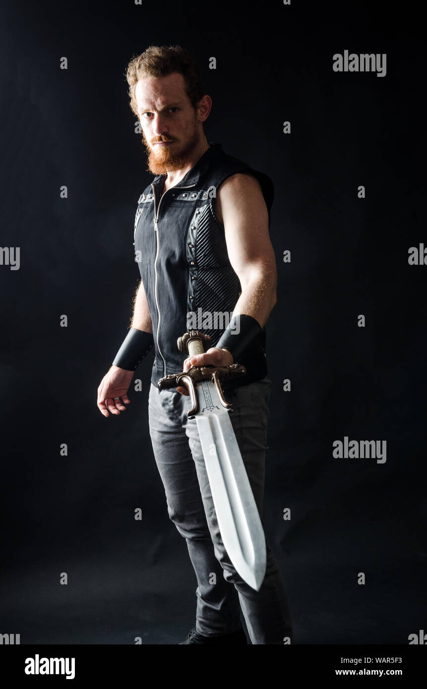 Portrait of a redhead young man with a sword and a knight coat on black ...