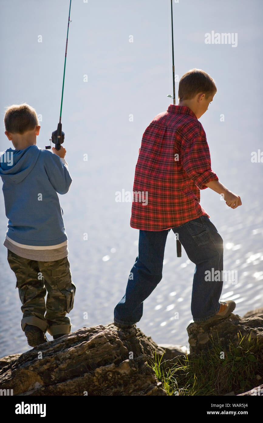 Two young brothers standing next to each other on a riverbank while ...