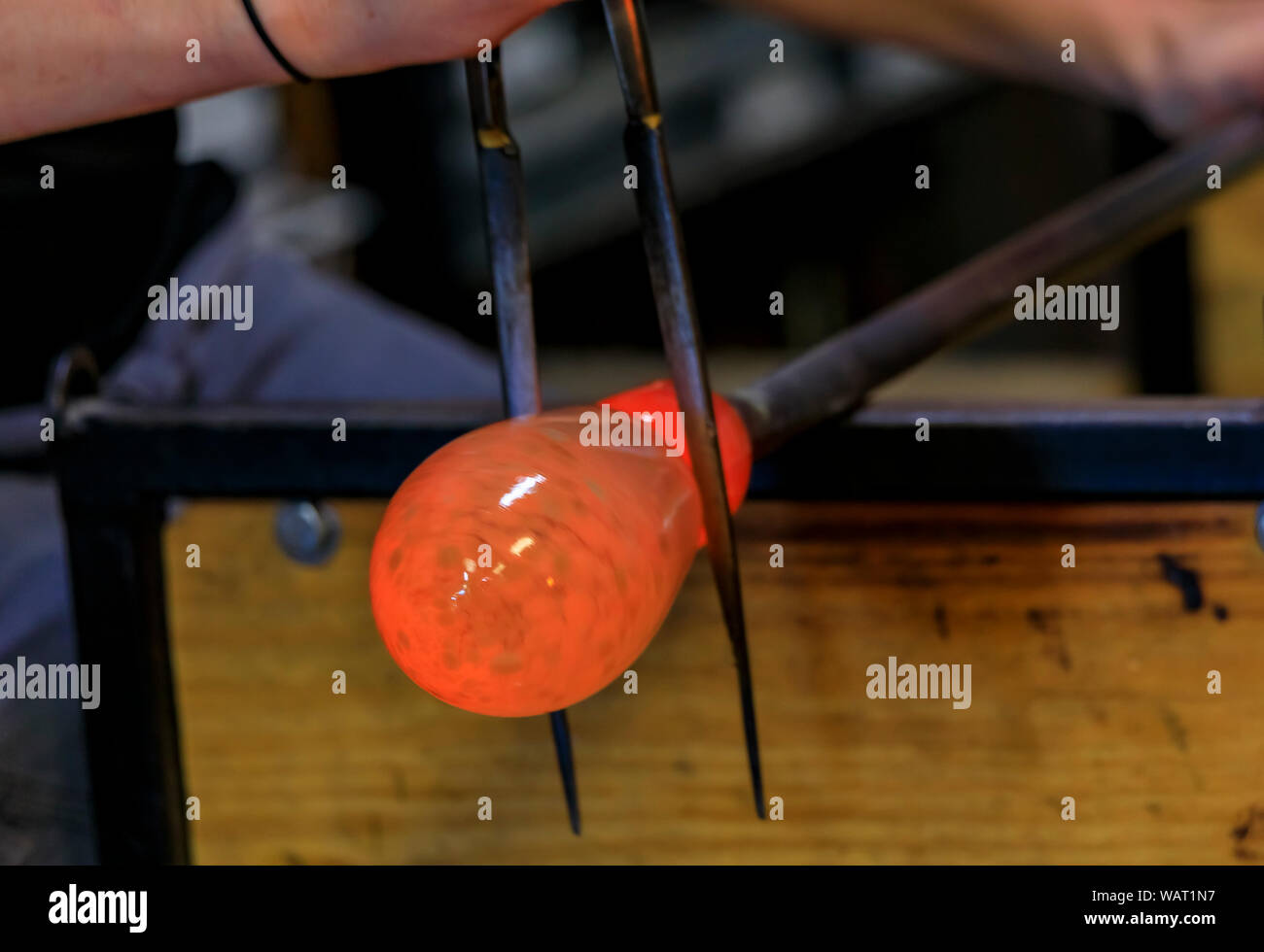 Glass blower shaping a bubble of melted glass on a rod by hand in the ...