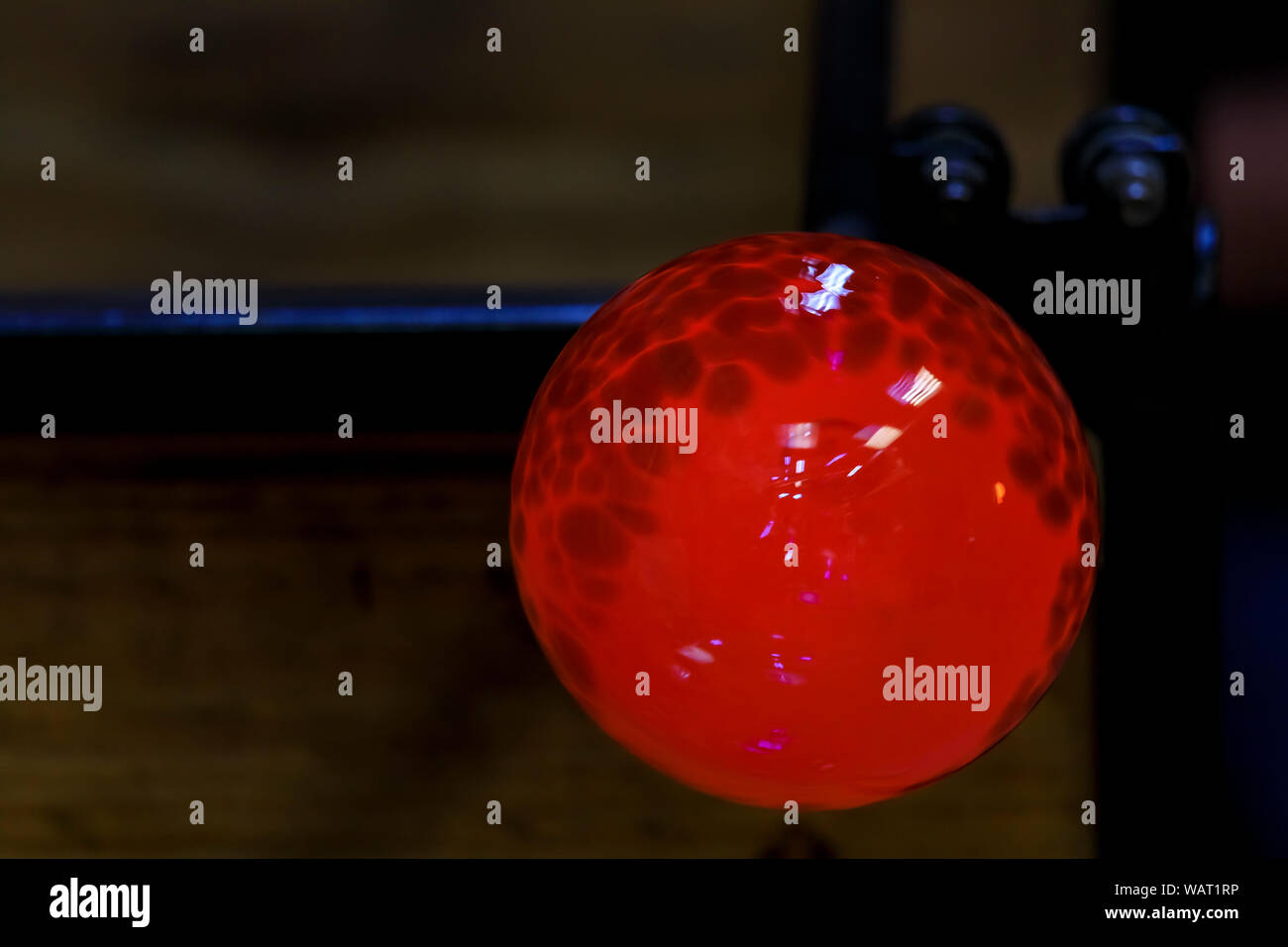 Glass blower shaping a bubble of melted glass on a rod by hand in the ...