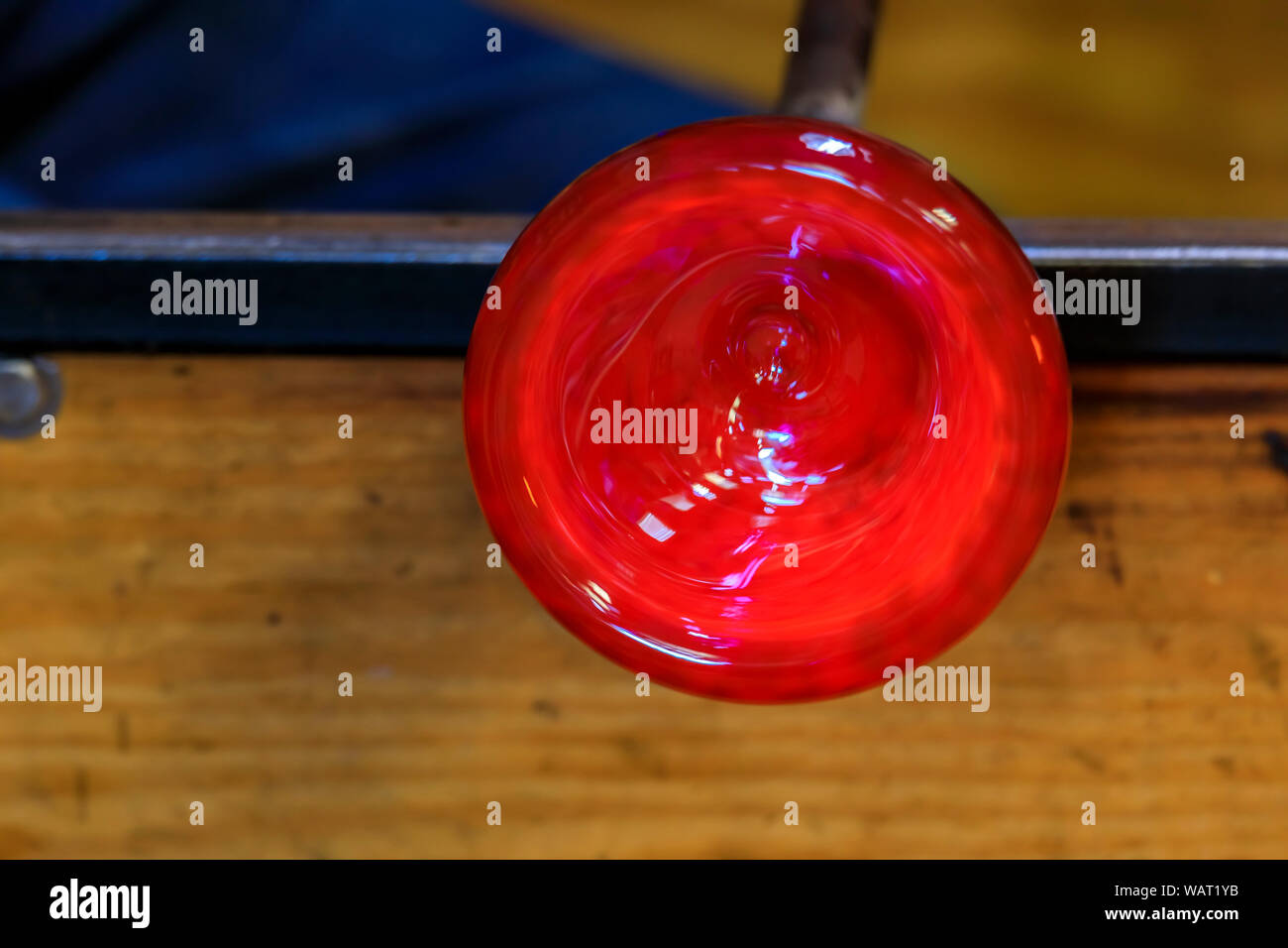 Glass blower shaping a bubble of melted glass on a rod by hand in the ...
