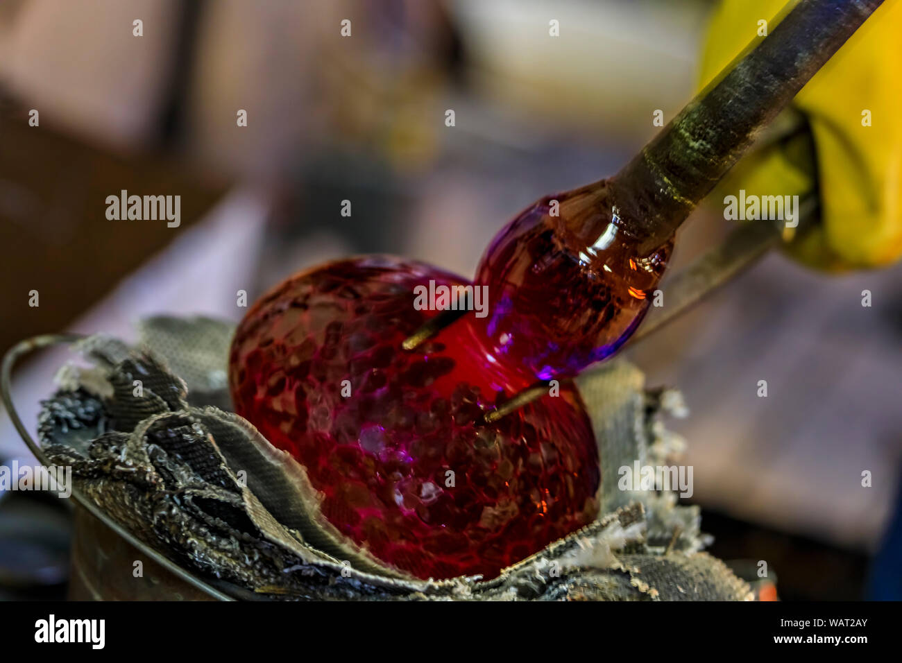 Glass blower shaping a bubble of melted glass on a rod by hand in the ...