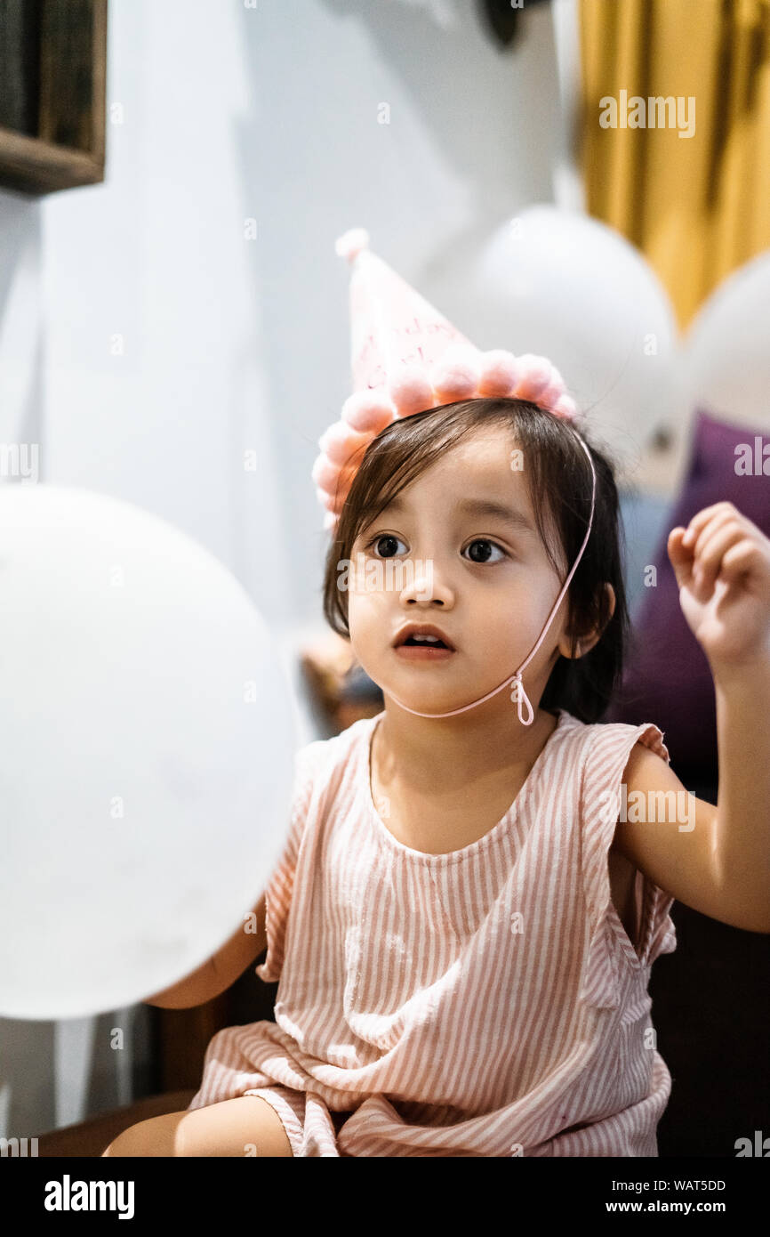 Asian toddler girl is celebrating birthday and wearing a pink hat and holding a baloon Stock ...