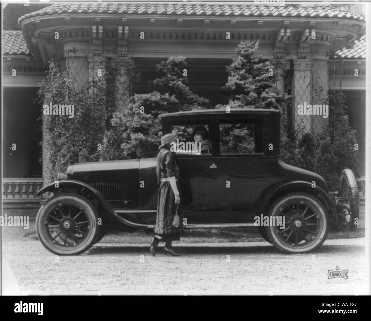 Driver's side view of 1920 Chandler, with a woman standing at the door ...