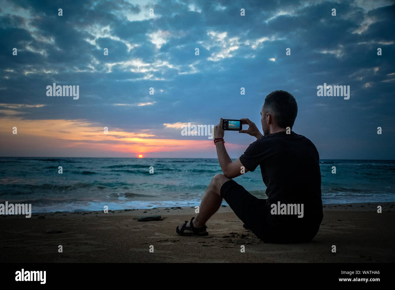 Young man using a cellphone on beach a ocean cliff during sunset ...