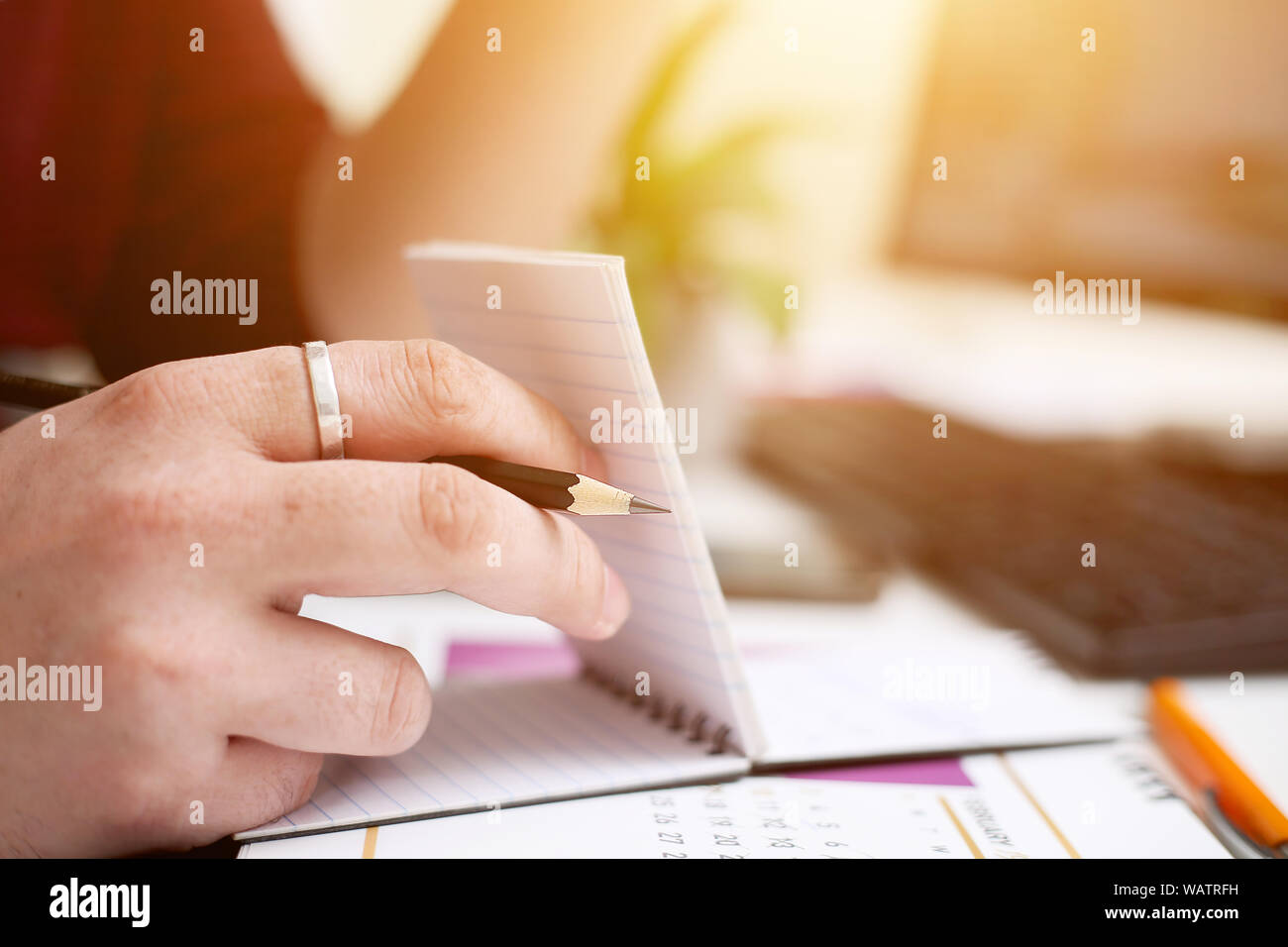 Picture of Man writing on a notebook with pen and holding mobile in ...
