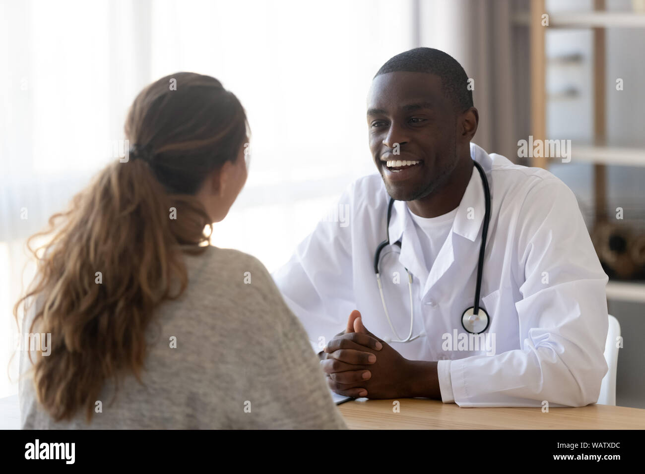 Smiling black male doctor listening female patient at medical meeting ...