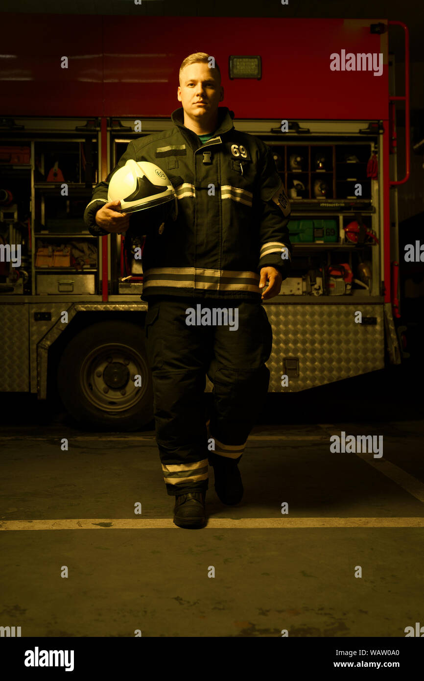 Full-length photo of young firefighter with helmet in his hand looking ...