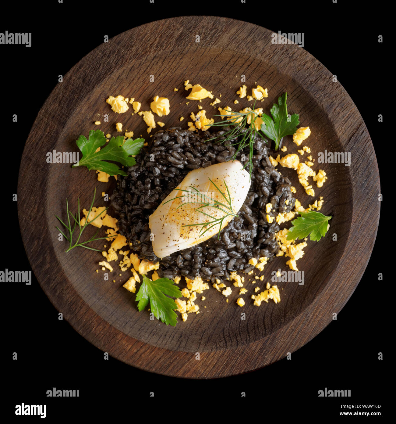 Black squid ink rice and fried calamar on wound wooden plate isolated ...