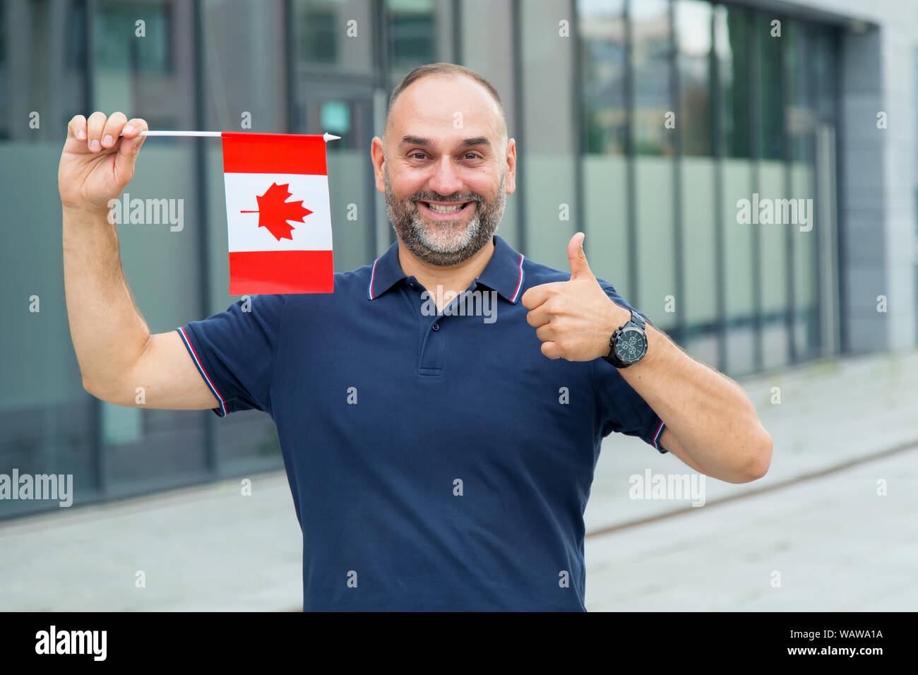 Portrait of a mature man with the flag of Canada shows thumb up gesture ...