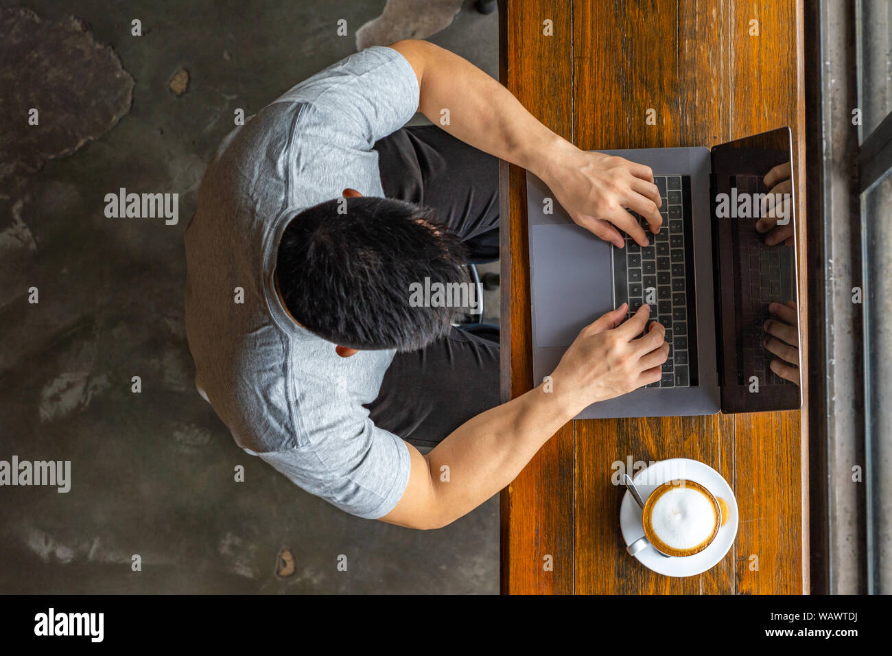 Muscled Asian man typing laptop next to cup of cappuccino Stock Photo ...