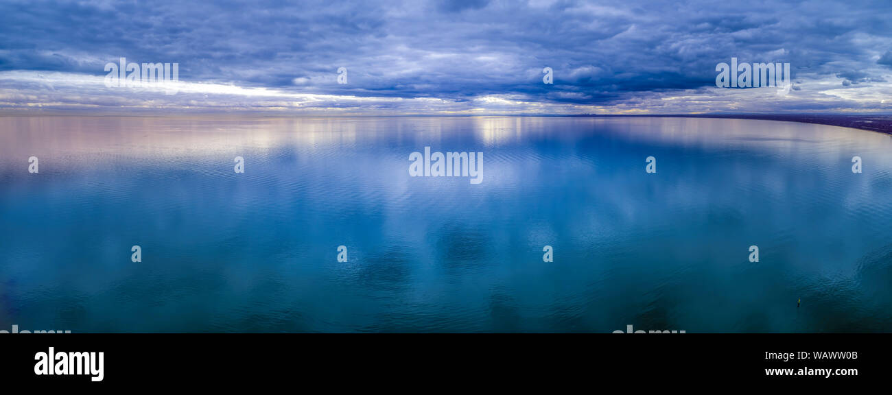 Wide aerial panorama of stormy clouds over smooth ocean water surface ...