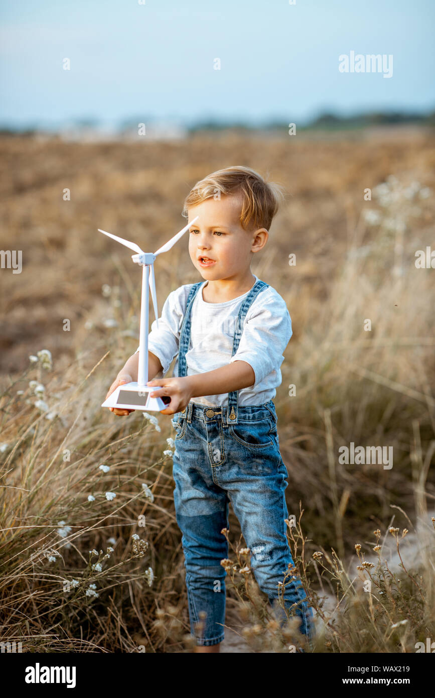 Curious young boy playing with toy wind turbine in the field, studying ...
