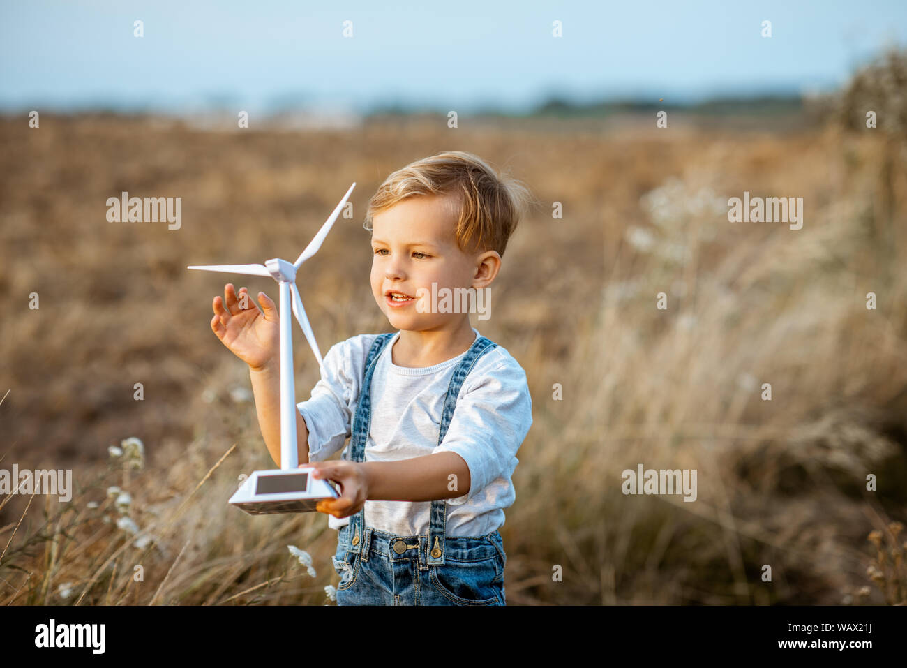 Curious young boy playing with toy wind turbine in the field, studying ...