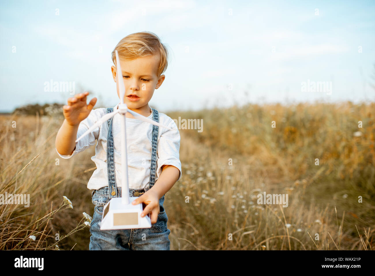 Portrait of a curious young boy playing with toy wind turbine in the ...