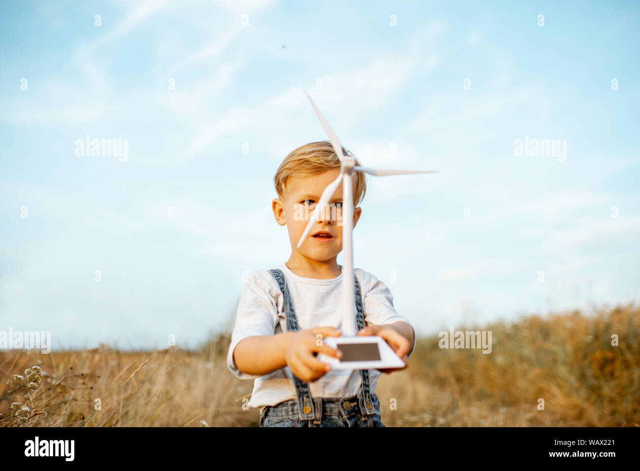 Portrait of a curious young boy playing with toy wind turbine in the ...