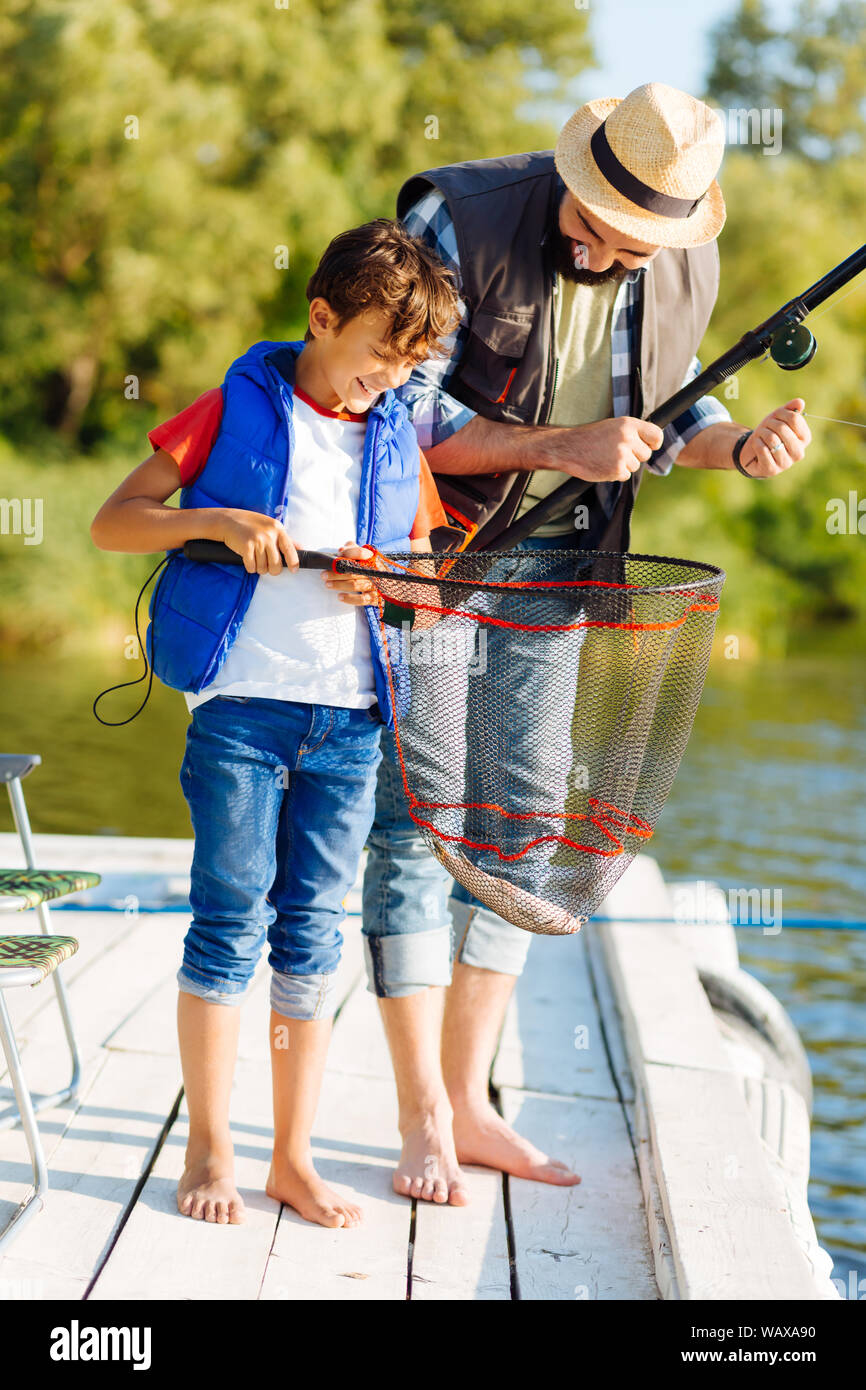 Son looking into fishing net after catching fish with father Stock ...
